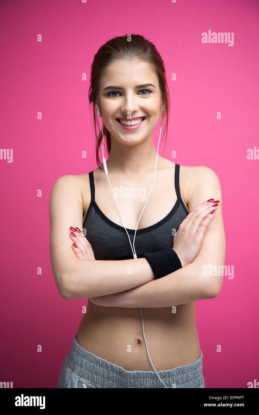 Smiling sports woman standing with arms folded over pink background ... Smiling sports woman standing with arms folded over pink background ...