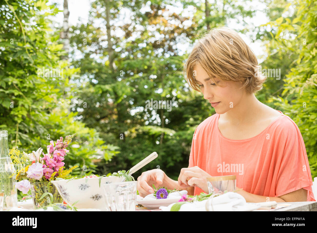 Young woman sitting at garden table pulling leaves from flower stem ...