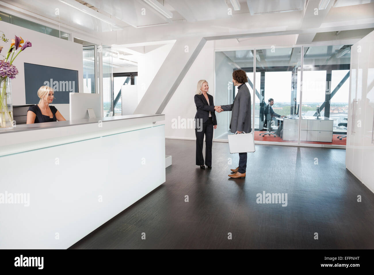 Woman shaking hands with visitor at reception Stock Photo - Alamy