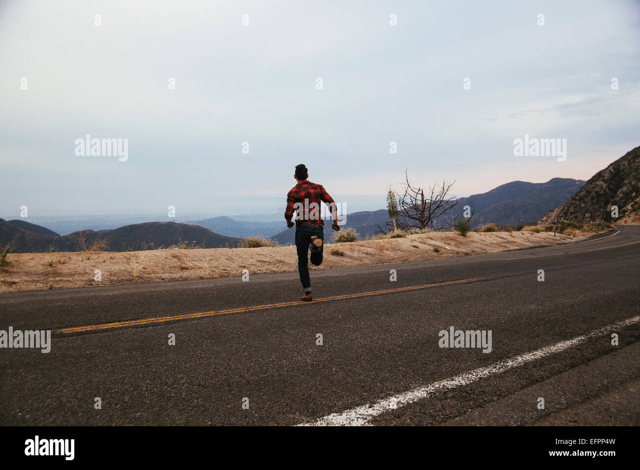 Young man running across mountain road, Los Angeles, California, USA ...
