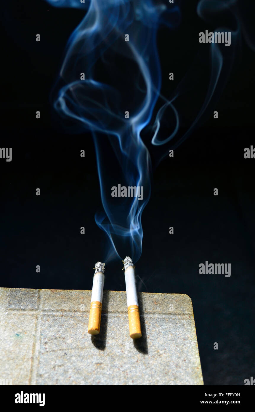 Two smoking cigarette on the table with dark background Stock Photo - Alamy