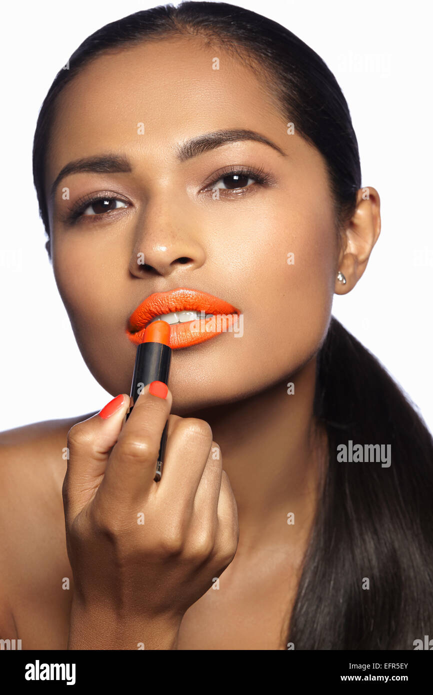 Female model applying orange lipstick Stock Photo - Alamy