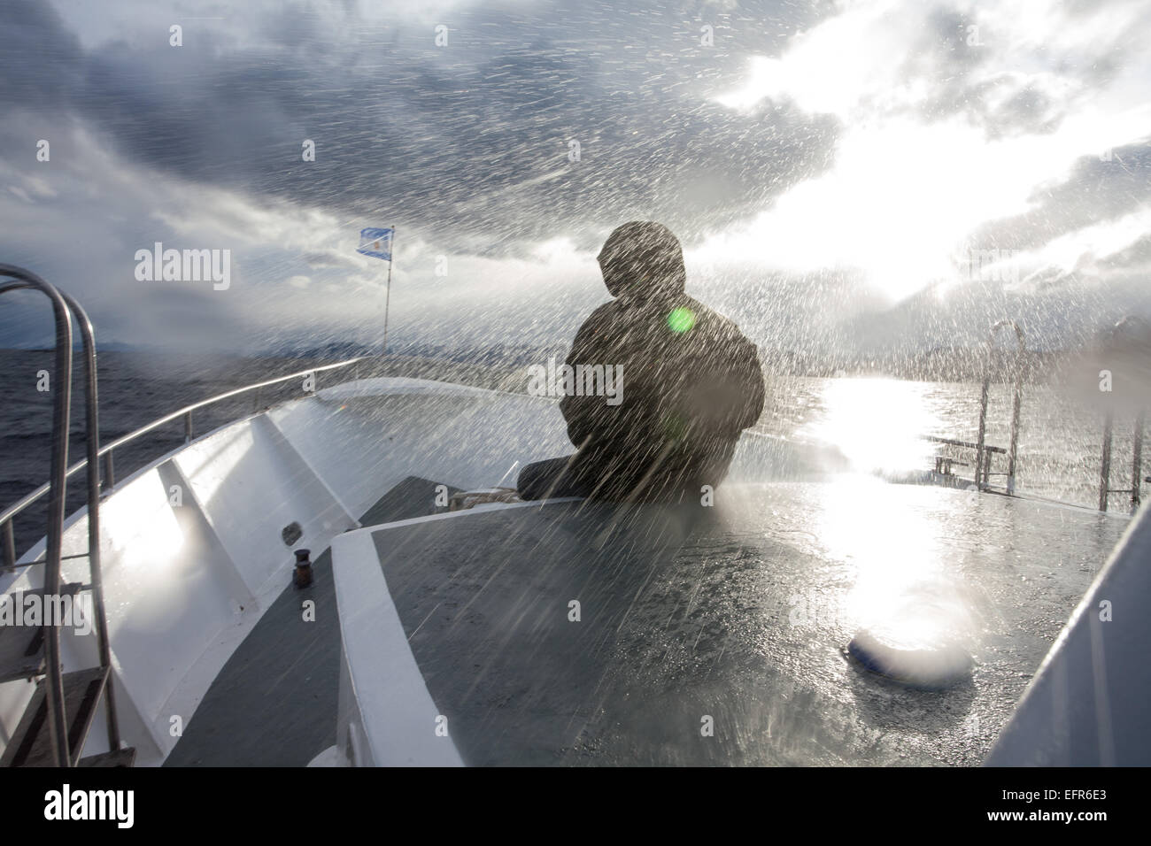 Person in waterproofs sitting in front of boat sailing in rain storm ...