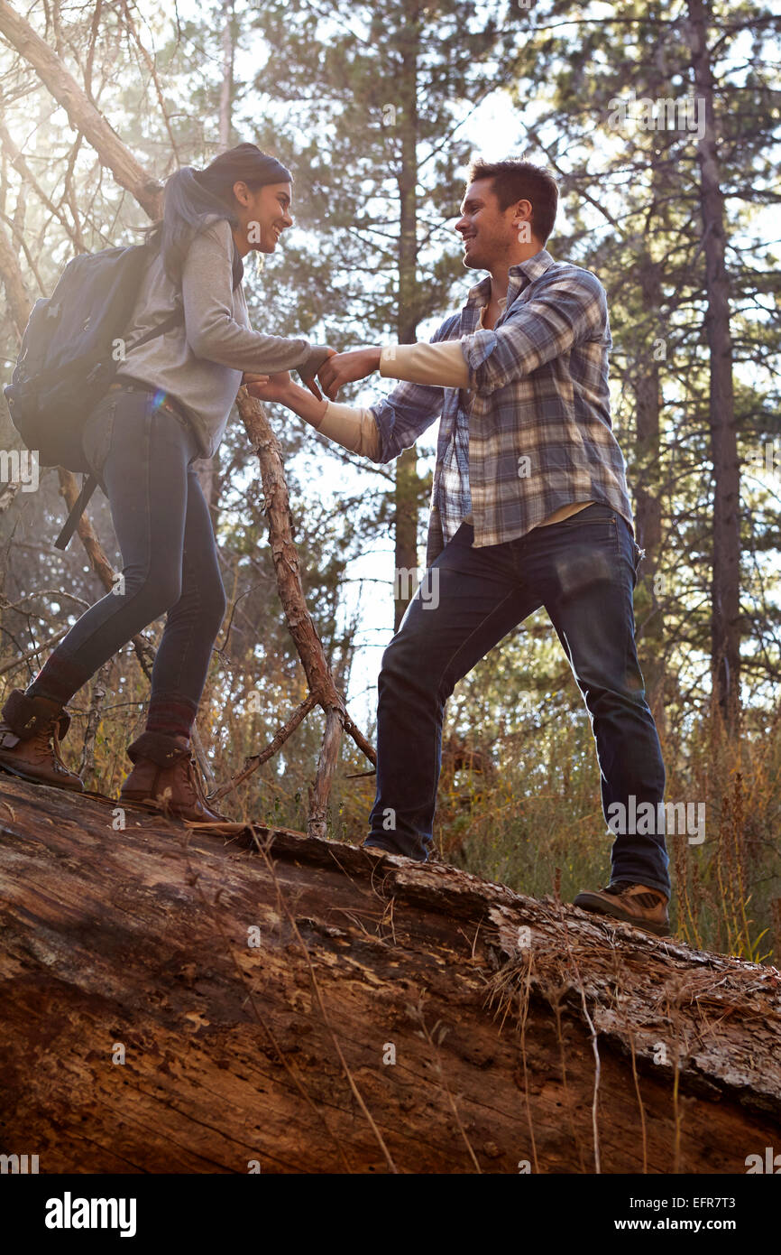Young man giving girlfriend a helping hand on fallen tree in forest ...