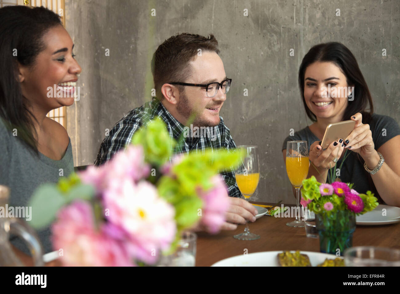 Friends at dinner table, young woman showing friend smartphone screen ...