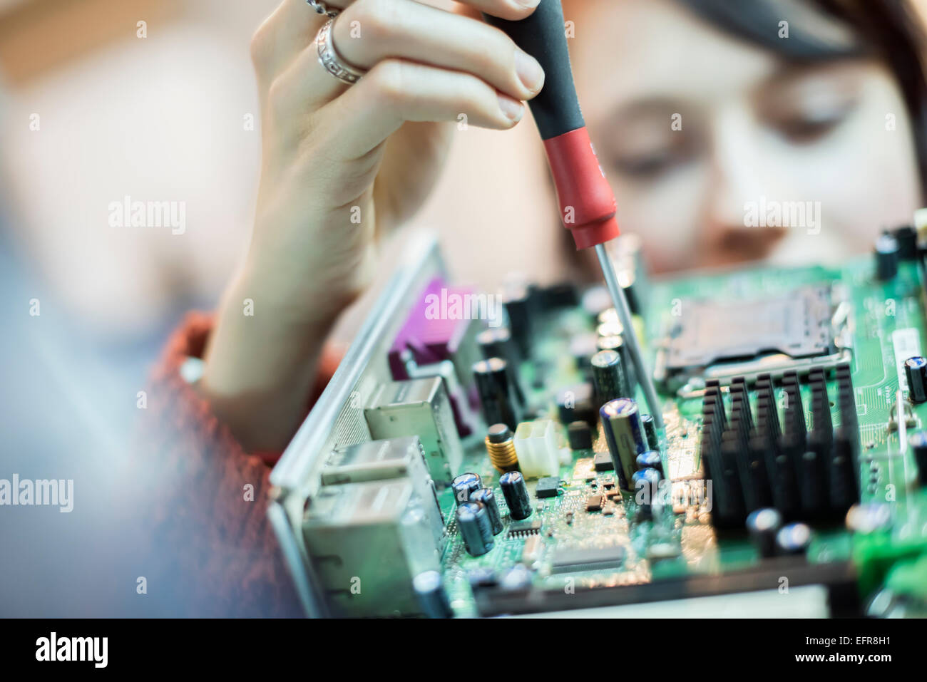 A woman using an electronic screwdriver on a computer circuitboard ...