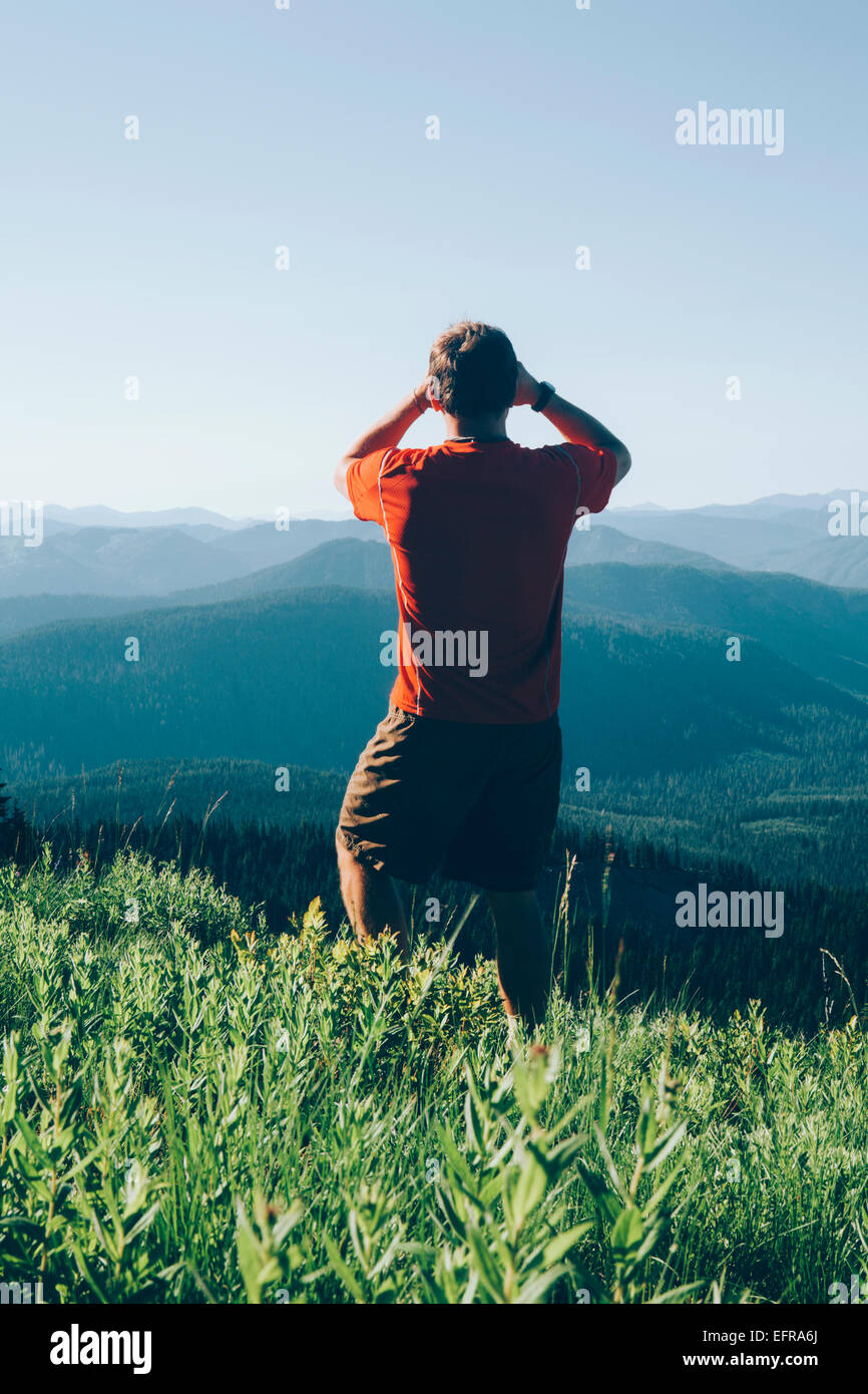 A man standing on a mountain ridge, taking a photograph of the ...