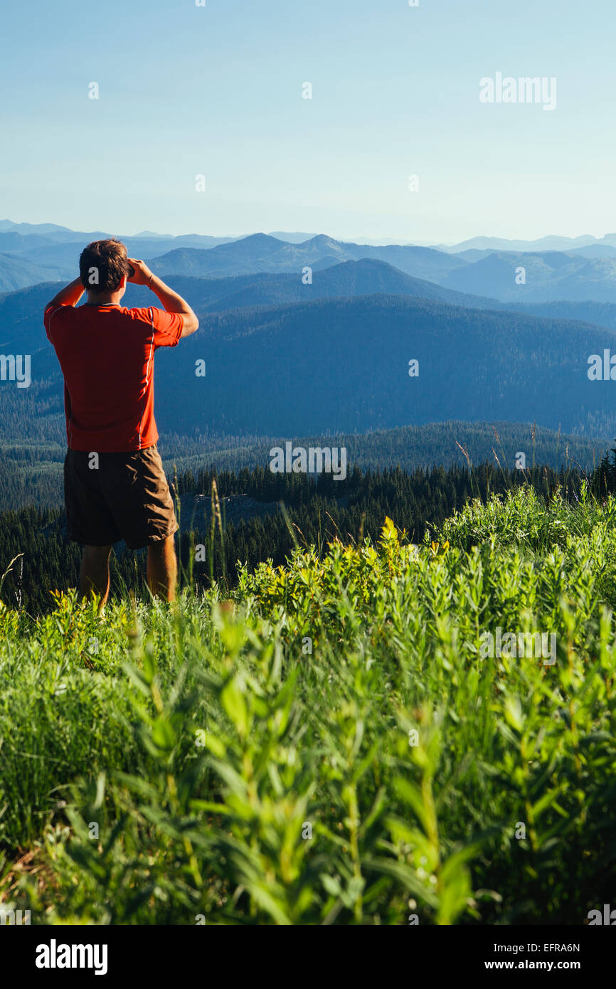 A man standing on a mountain ridge, taking a photograph of the ...