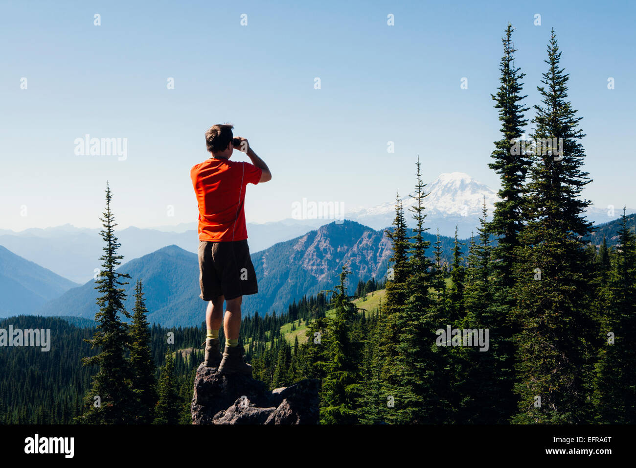 A man standing on a mountain ridge, taking a photograph of the ...