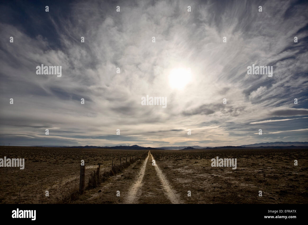A big sky with clouds over the prairie, and a dirt road track leading ...