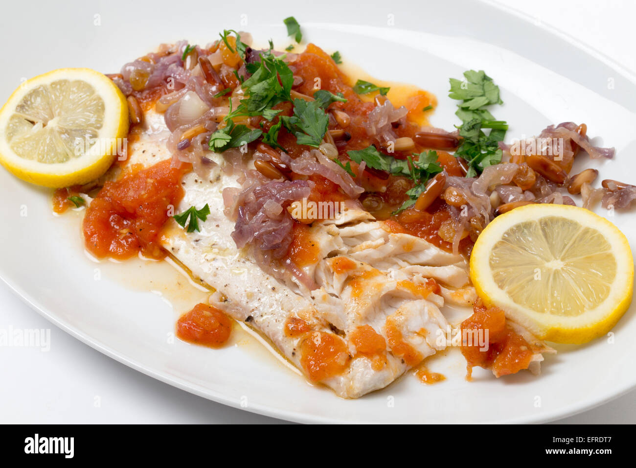 Baked fish in tomato sauce with onion and pine nut garnish, a ...