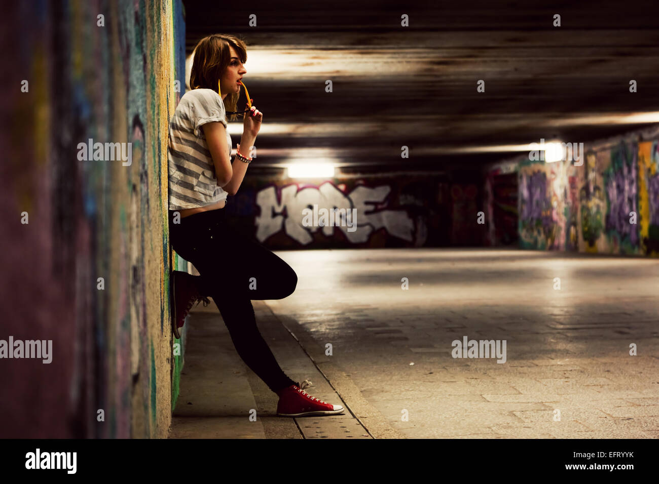 Stylish young girl standing in grunge graffiti tunnel, shanty town ...