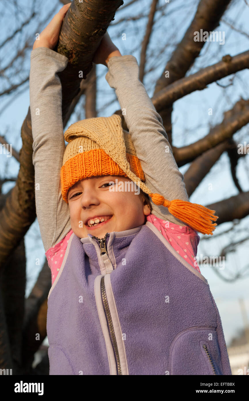 Young girl swinging on a tree branch in the autumn wearing knitted ...