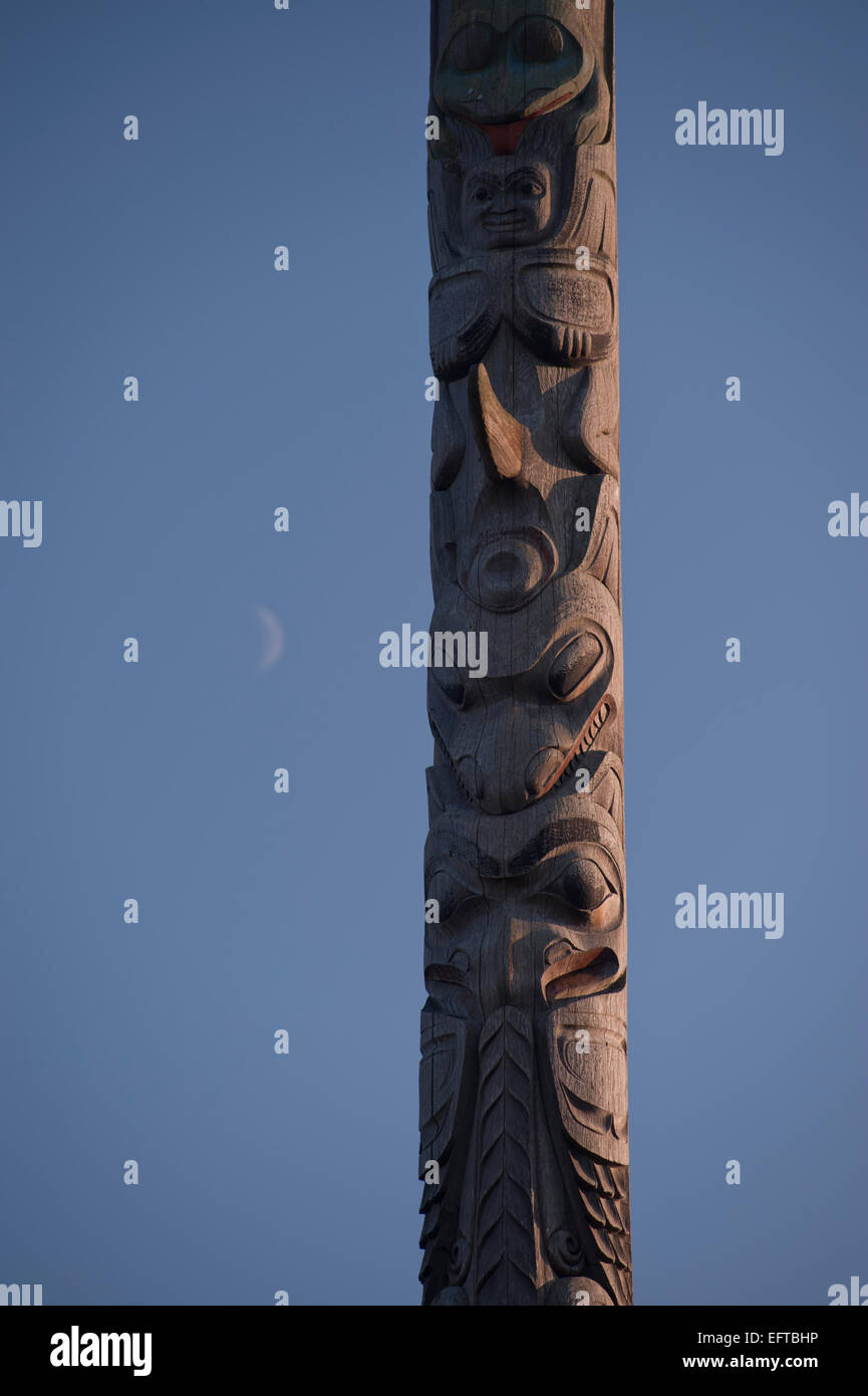 A setting sun illuminates a totem pole with a new moon in the ...