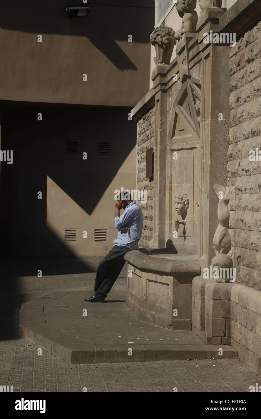 Man on mobile cell phone, standing by old stone drinking fountain in ...