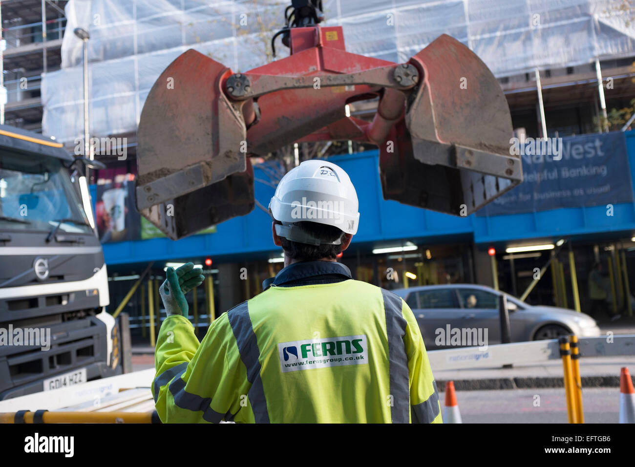 A workman man manoeuvres a digger into position, and as he does so it ...
