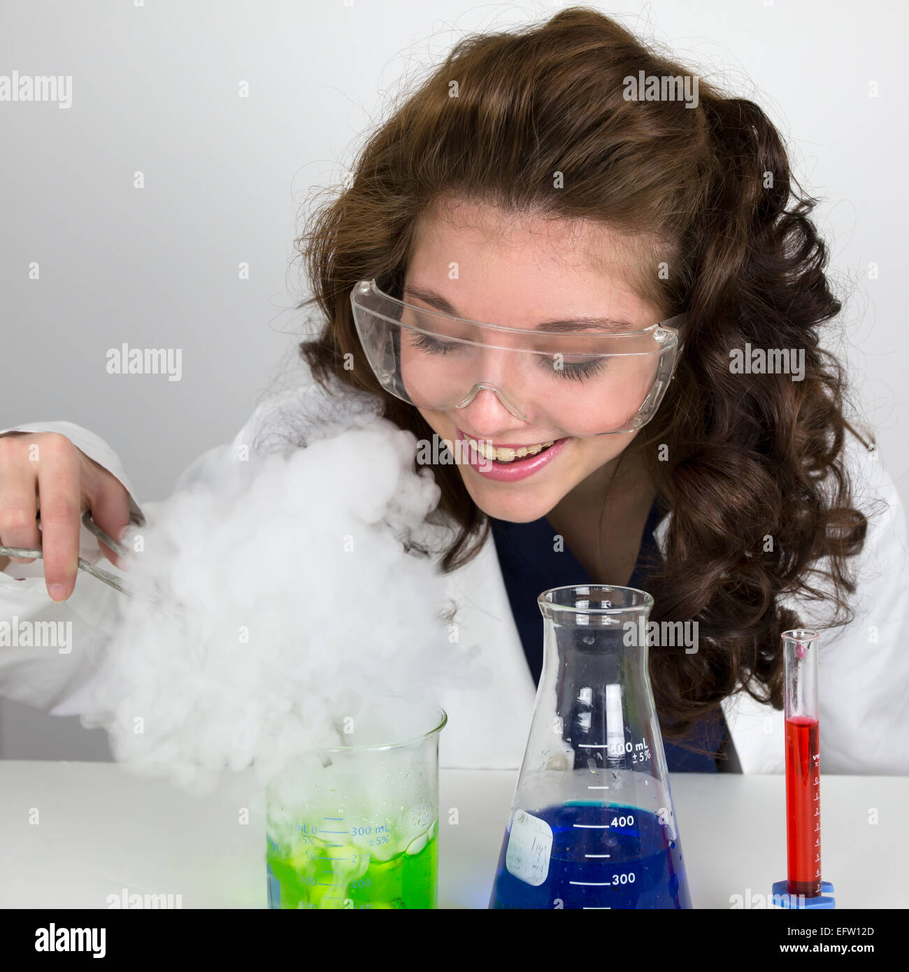 Teenage girl wearing lab coat and doing a science experiment with green ...