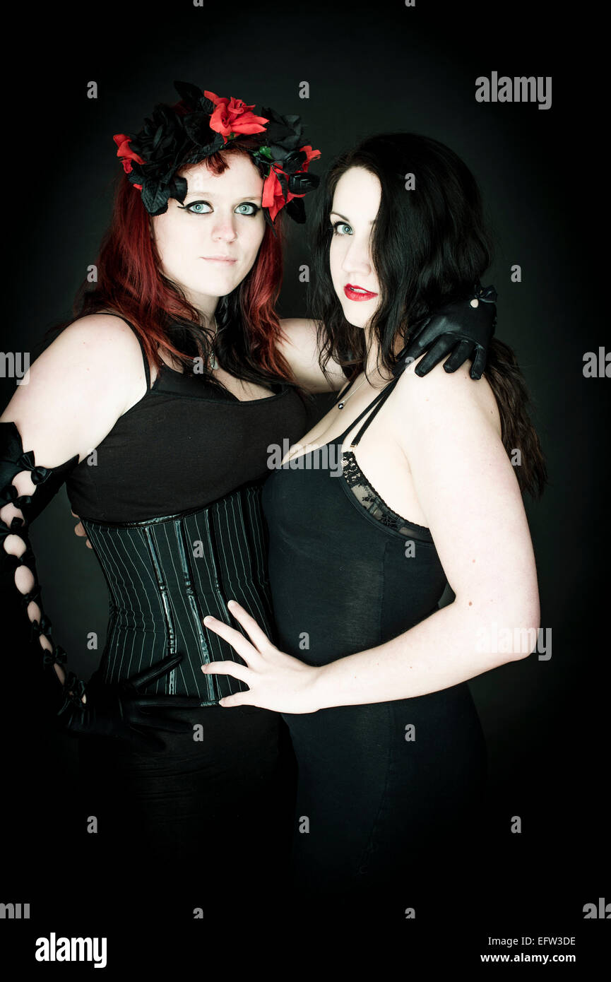Two young green-eyed goth gothic girl women dressed in black, a couple ...