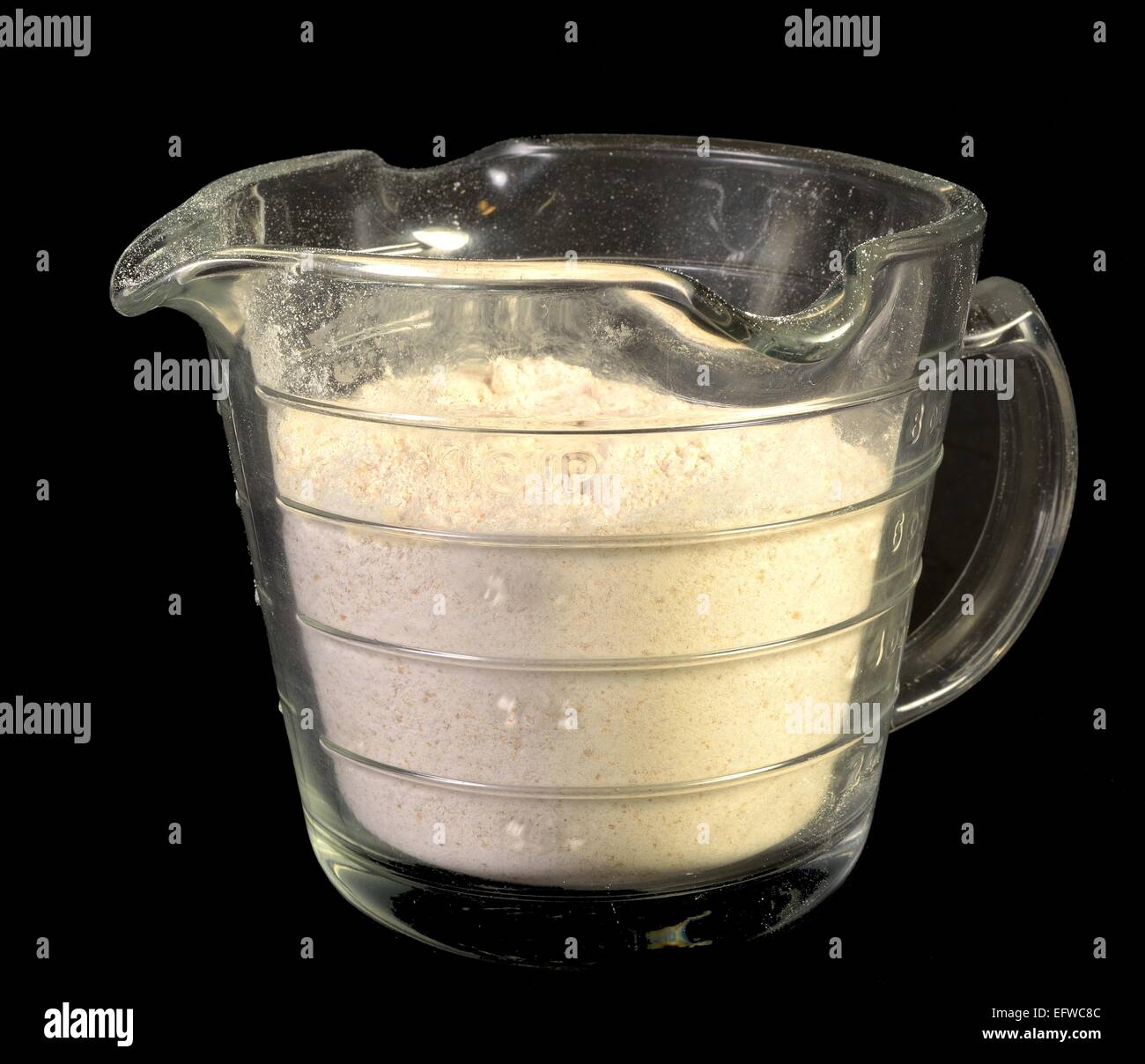 Measuring cup three quarters filled with flour on a black background ...