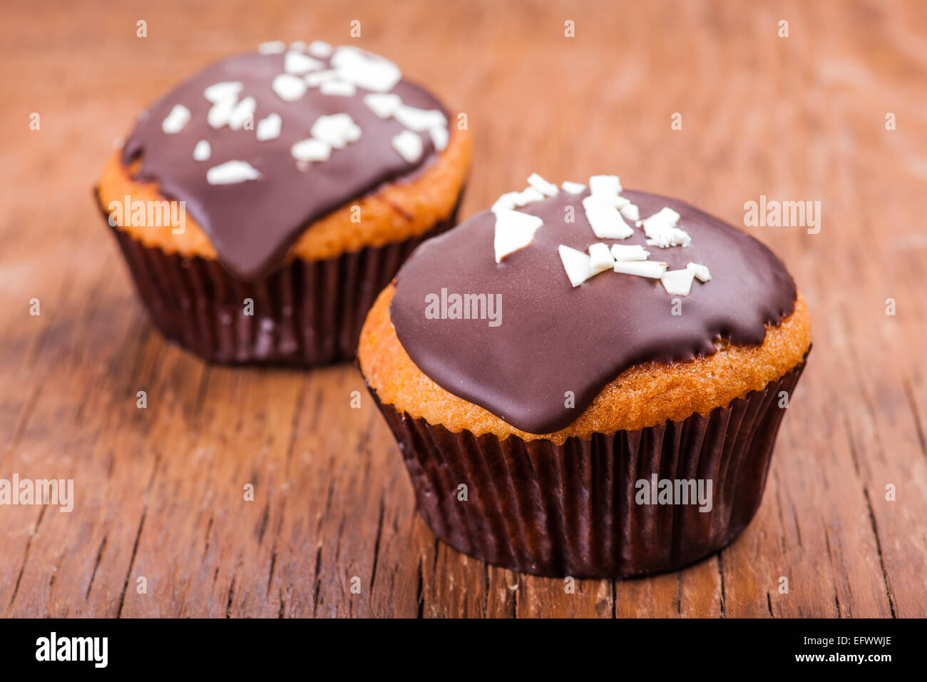 two cupcakes in chocolate icing on a wooden background Stock Photo - Alamy