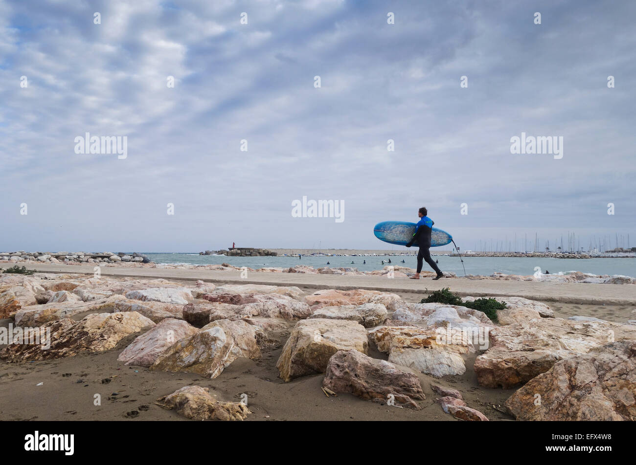 Surfer walks up a stone pier to surf the waves during bad weather and ...