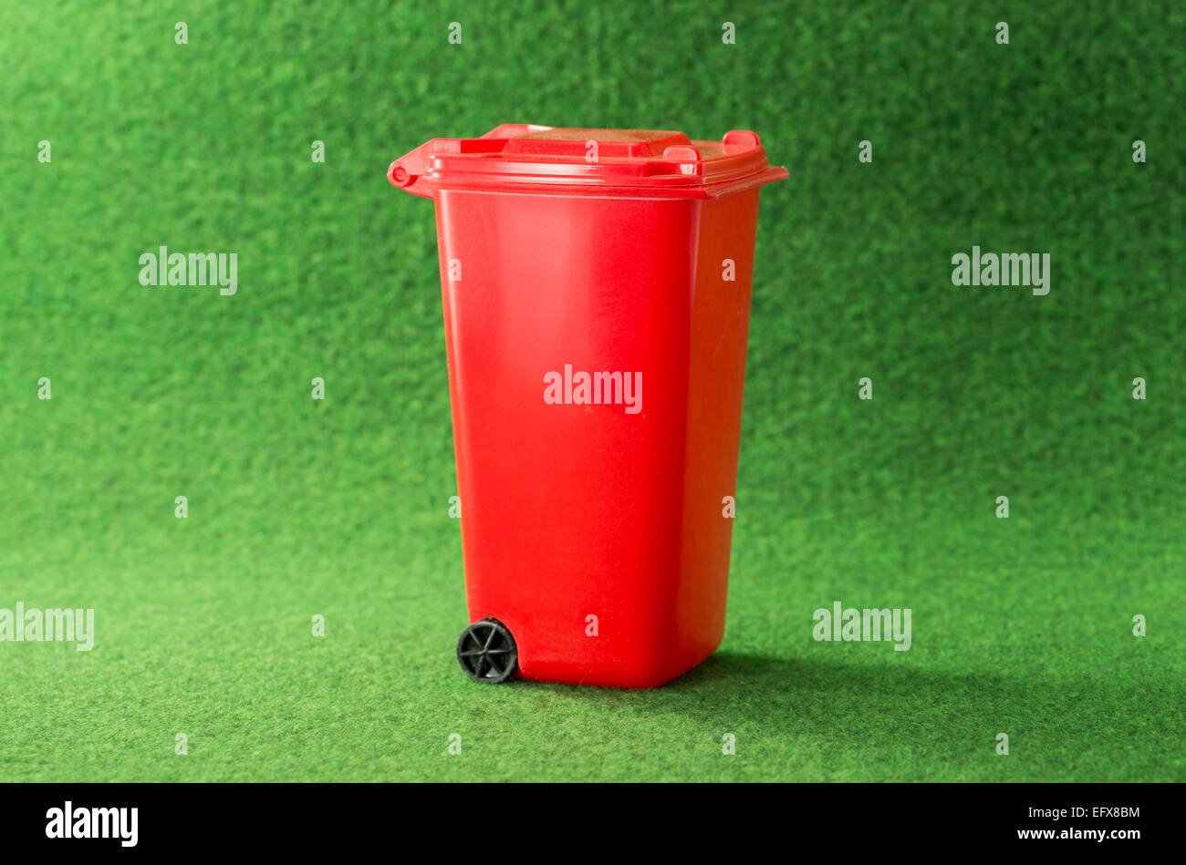 red closed garbage bin container on green background Stock Photo - Alamy
