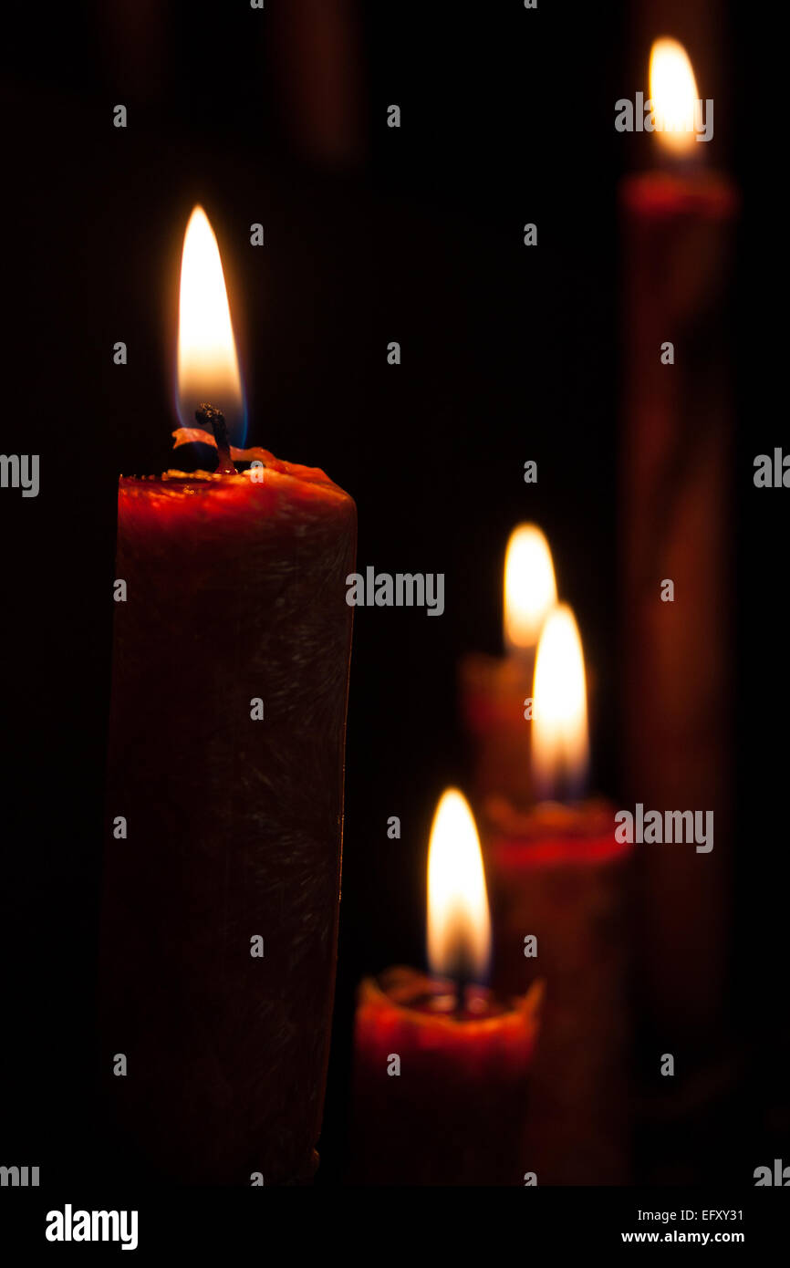 a group of five candles, all are lit with flame, and burning in a dark ...