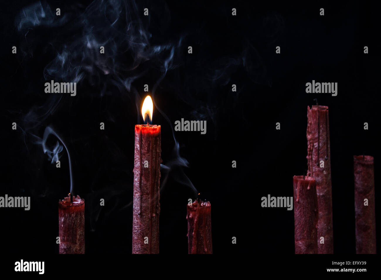 one candle is lit among other candles that have been blown out ...