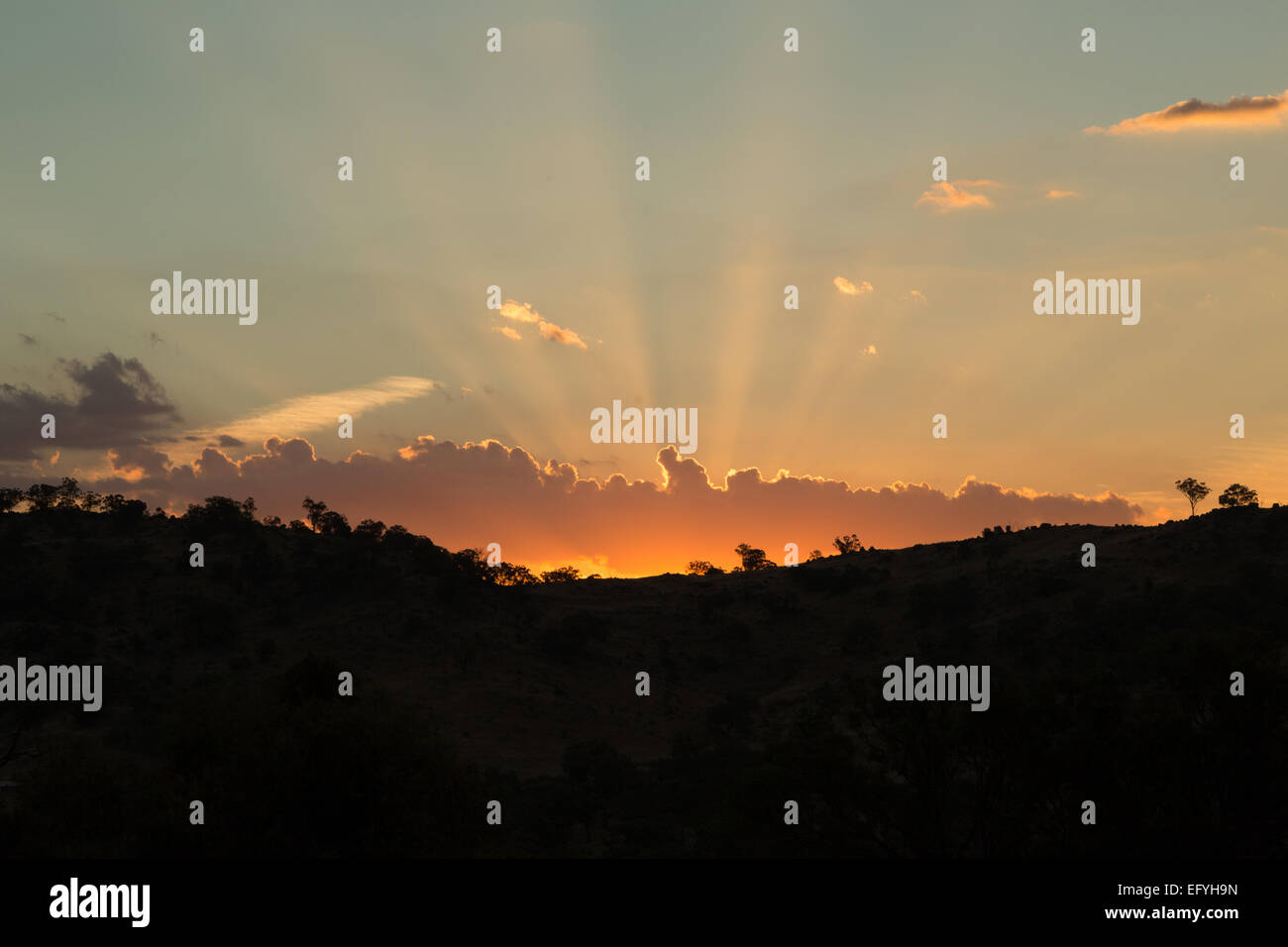 An unedited (RAW) photograph of the sun setting behind some hills. The ...