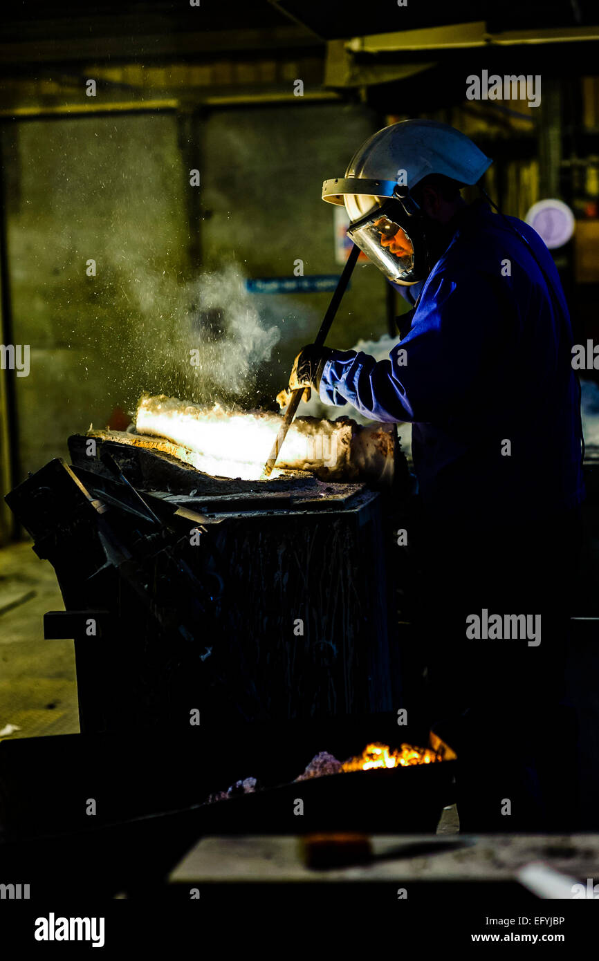 Foundry workers pour molten metal from a furnace using a crucible into ...