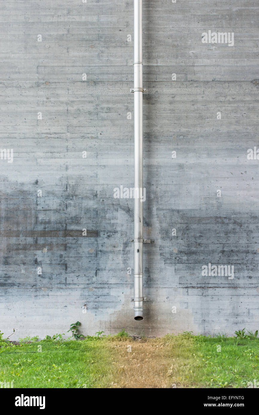 Urban scene with pipe on grey concrete wall and polluted grass ...