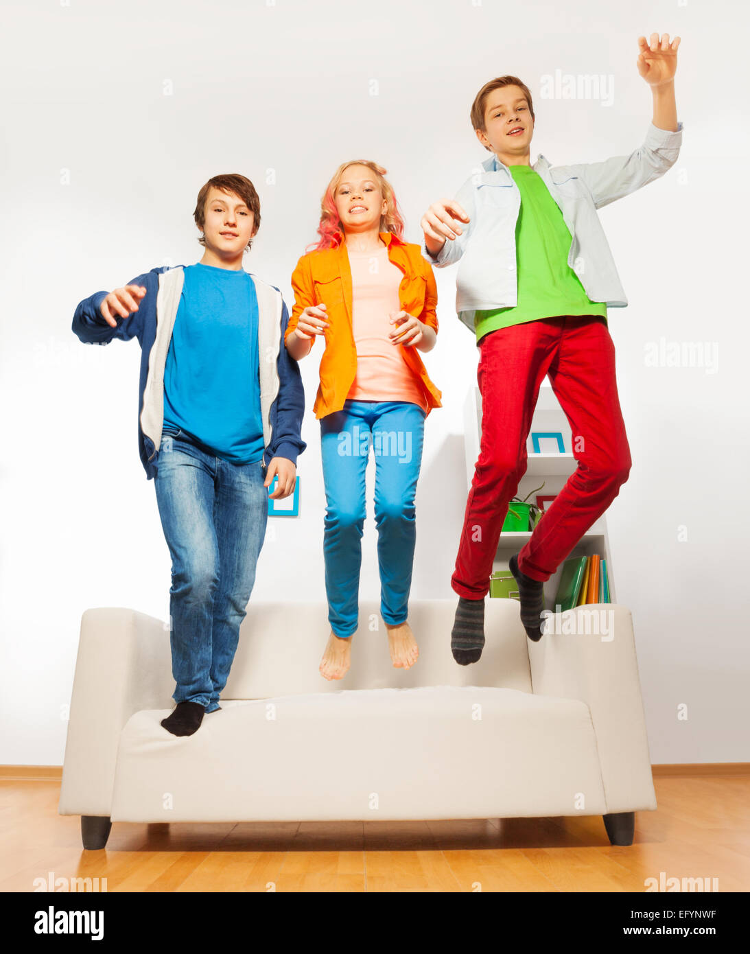 Three happy friends jumping on white sofa Stock Photo - Alamy