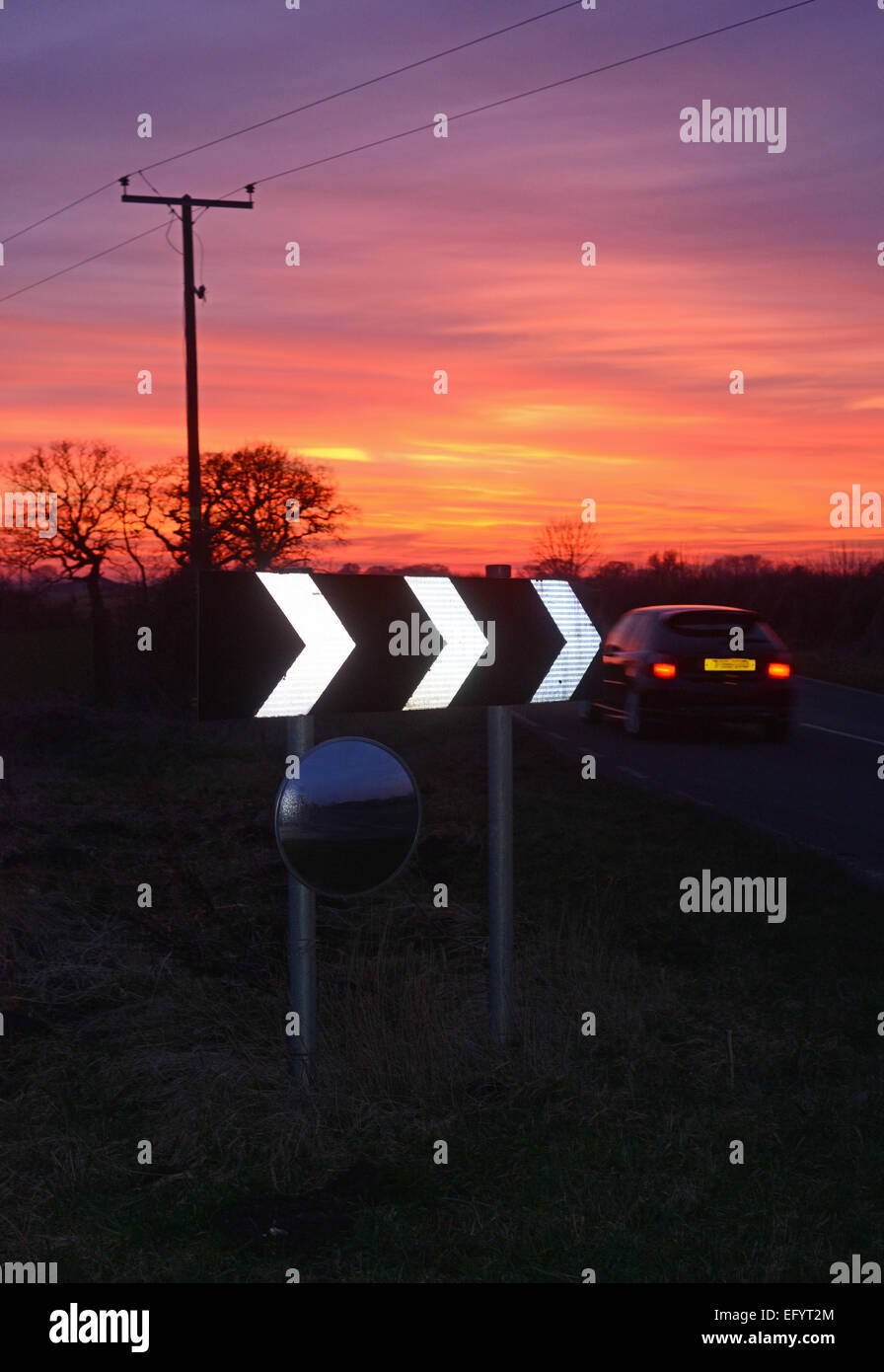 car at sunset passing warning sign of sharp bend and circular safety ...