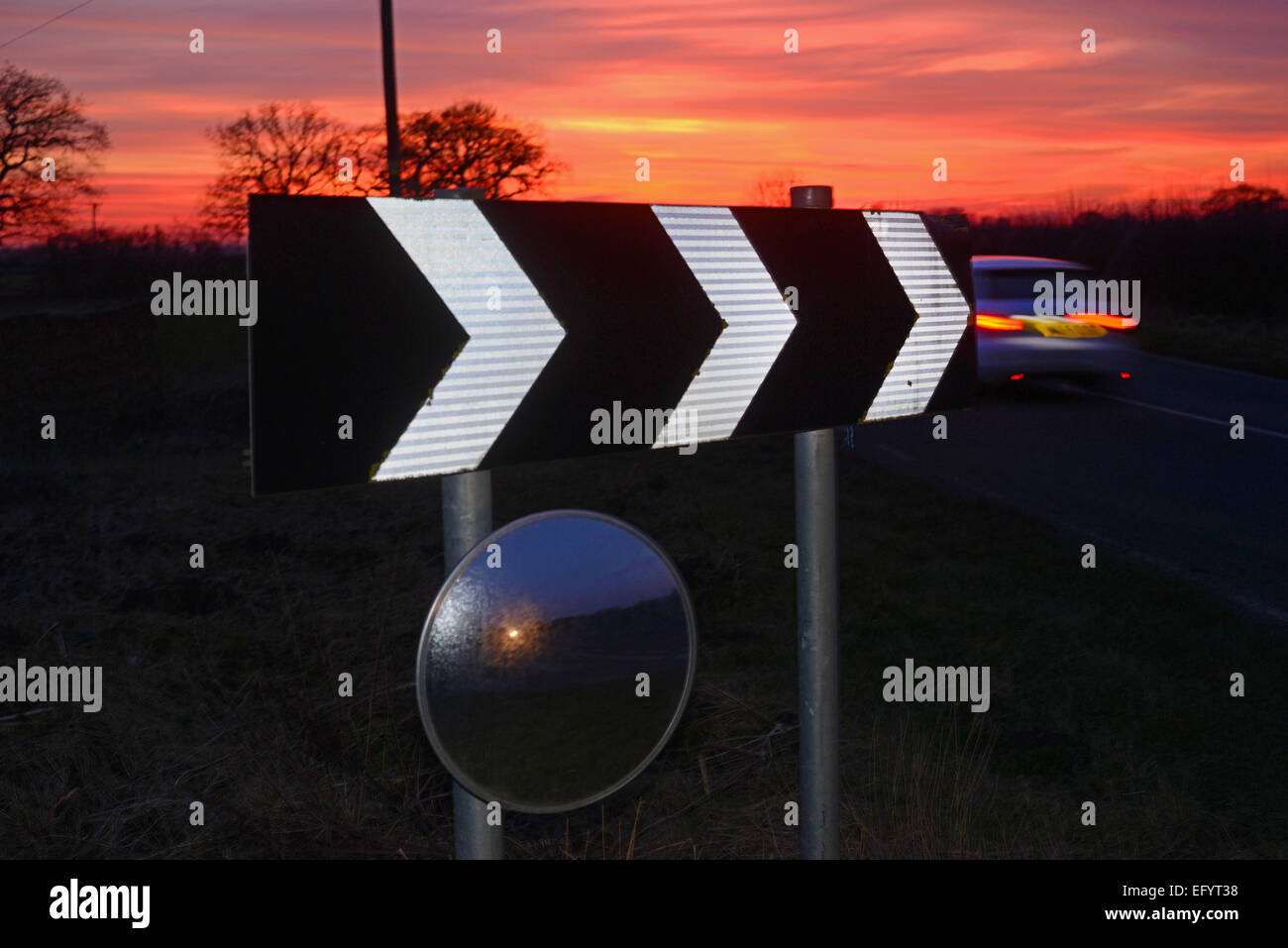 car at sunset passing warning sign of sharp bend and circular safety ...