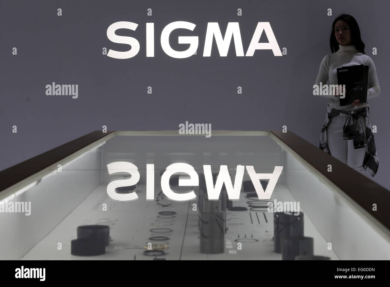 Tokyo. 12th Feb, 2015. A booth assistant stands next to a logo of Sigma ...