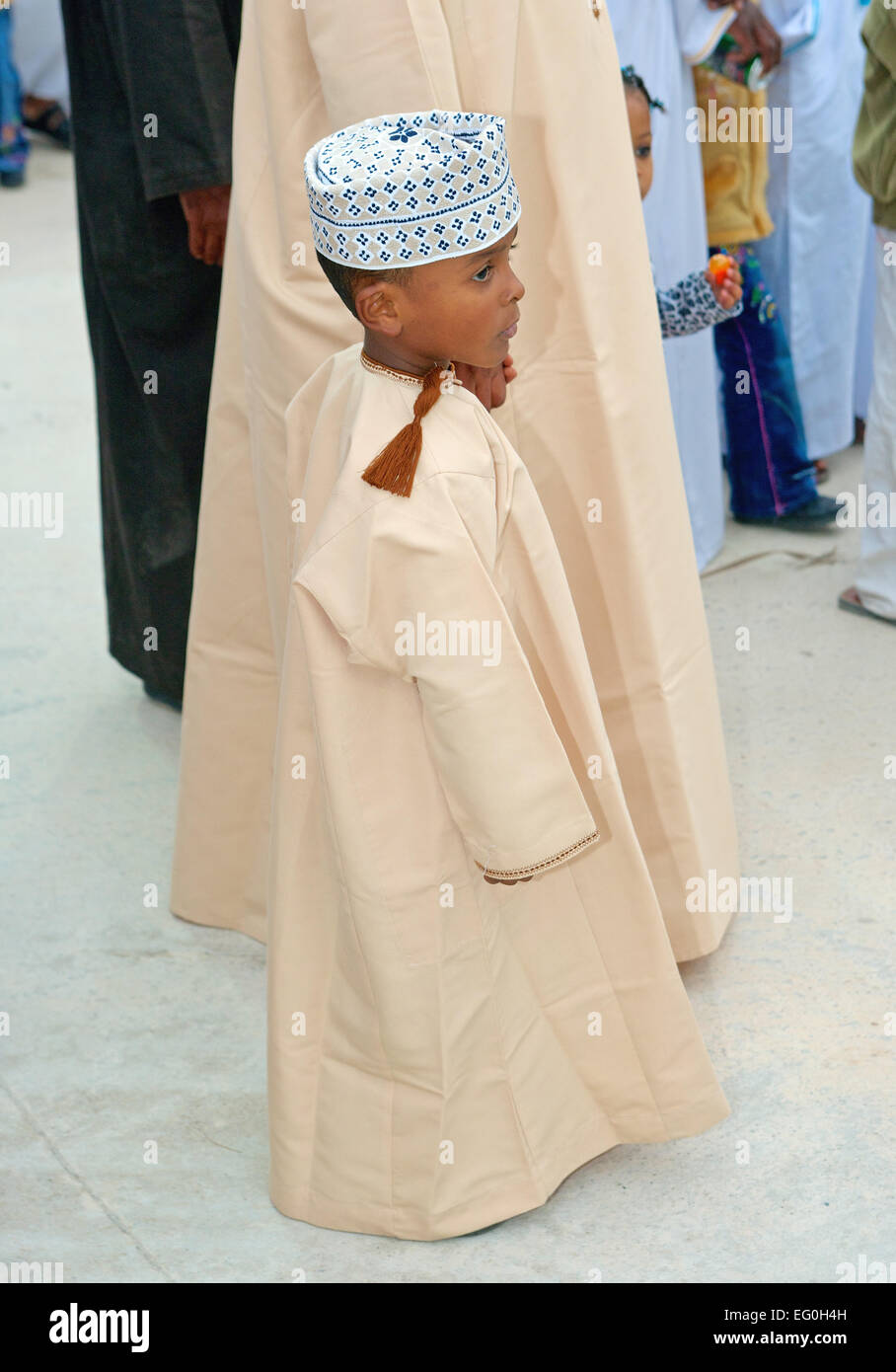 A young Omani boy, immaculately dressed in traditional clothing, holds ...
