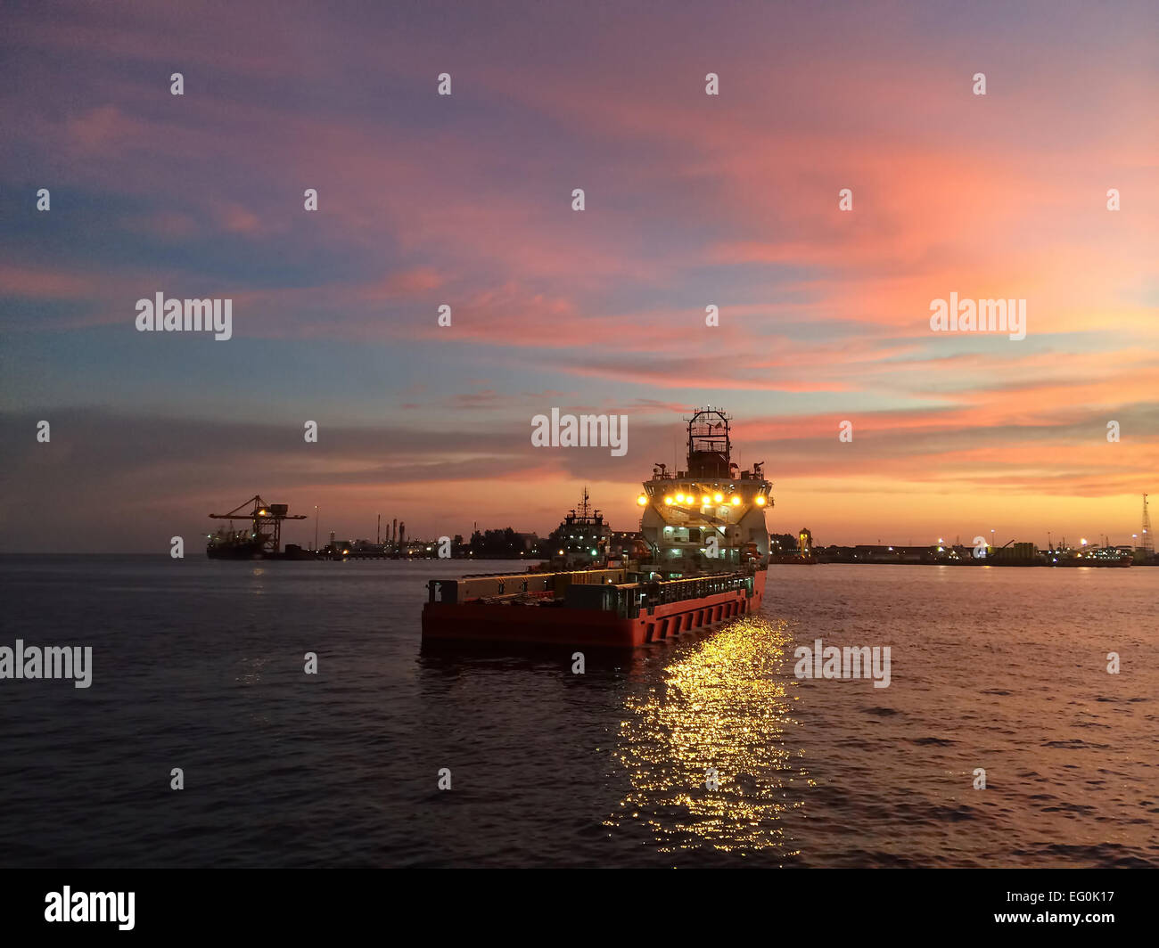 Illuminated oil rig support vessel arriving at port harbor at dusk ...