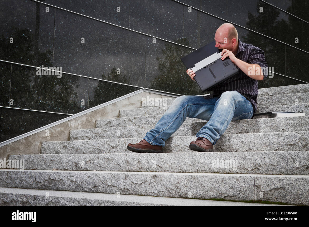 A angry man bites his computer / laptop in the stairs Stock Photo - Alamy
