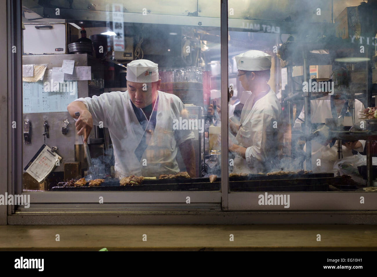 A chef working on the grill cooking yakitori seen through a steamed up ...