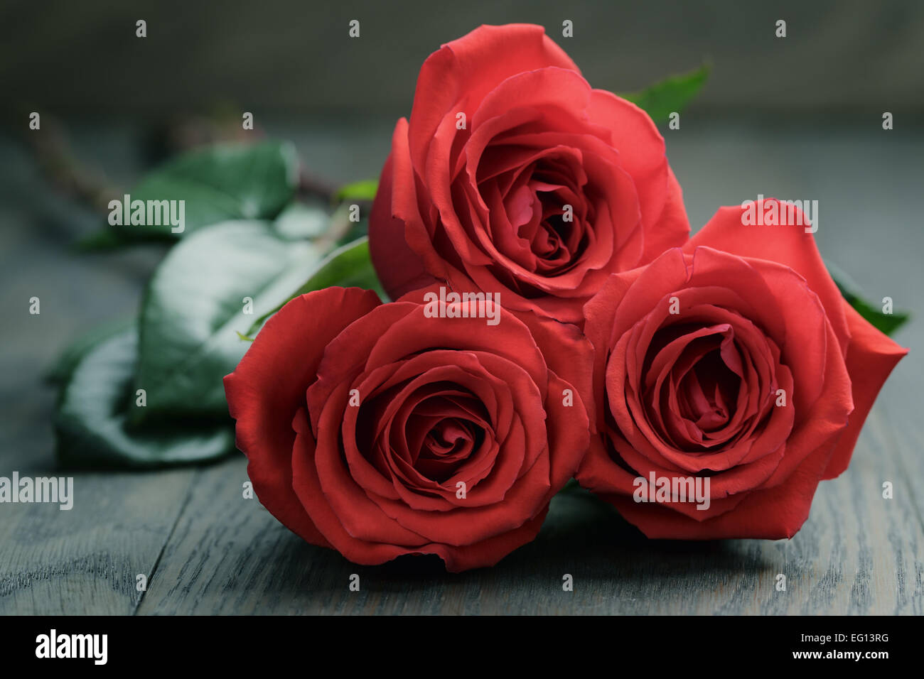 three red roses on old oak table Stock Photo - Alamy