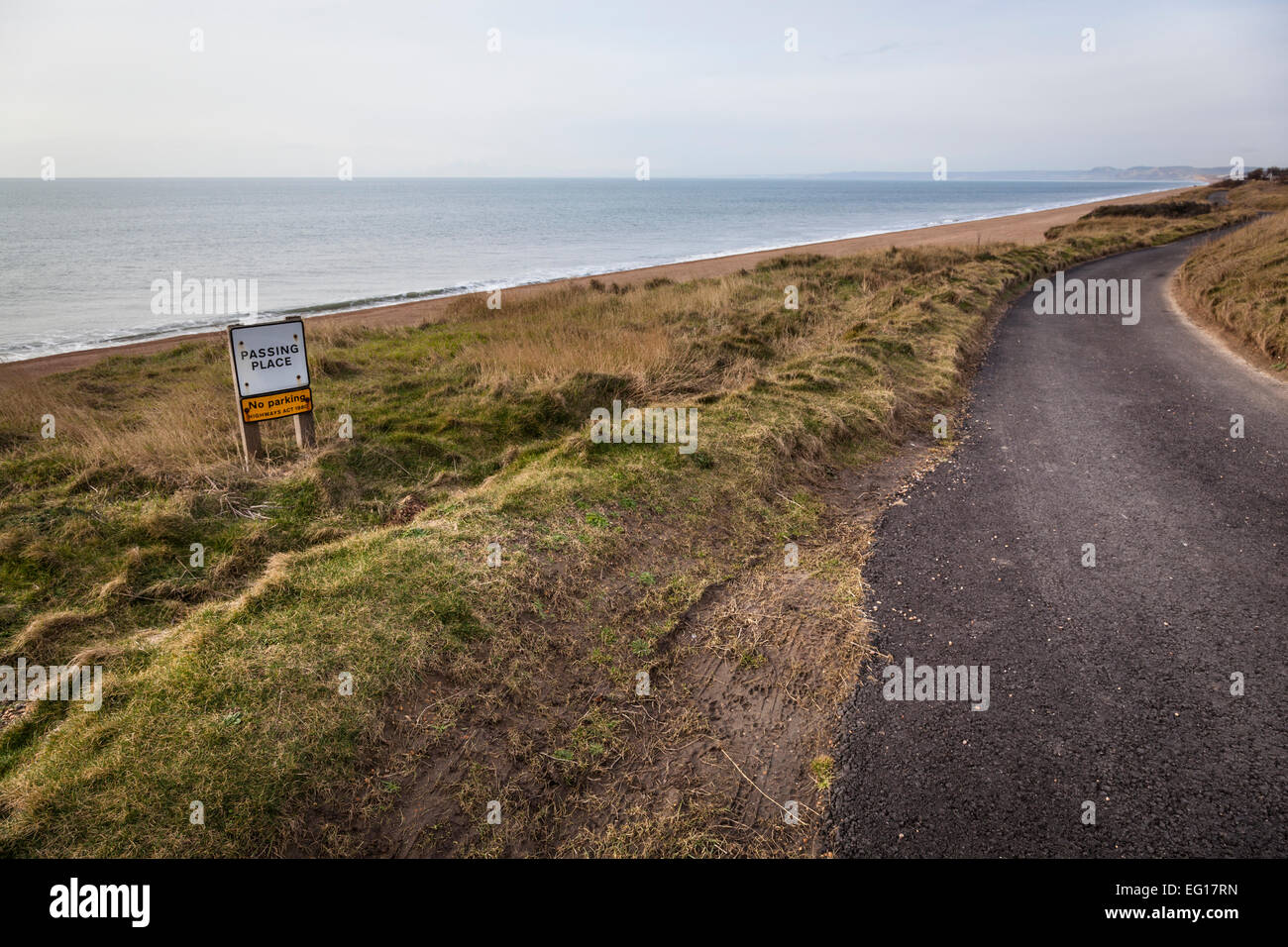 Narrow coastal road with passing place sign alongside Chesil Beach with ...