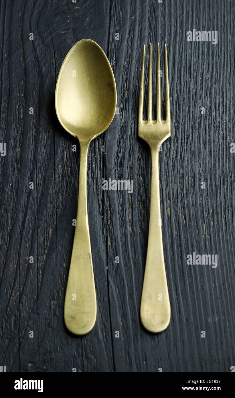 Golden spoon and a fork over black wooden table, top view Stock Photo ...