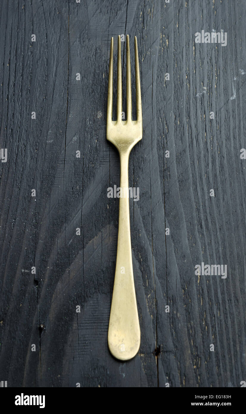 Single Golden fork over black wooden table, top view Stock Photo - Alamy