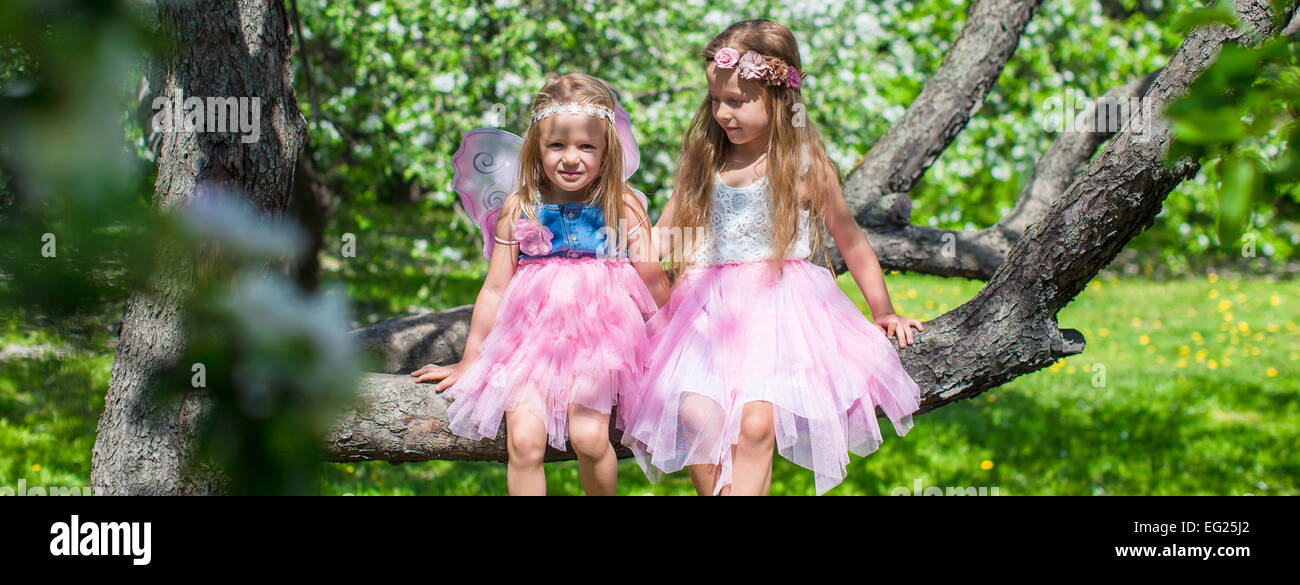Little adorable girls sitting on blossoming tree in apple garden Stock Photo - Alamy