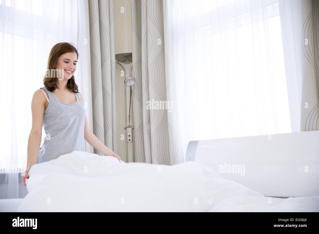 Portrait of a happy young woman making the bed at home Stock Photo - Alamy
