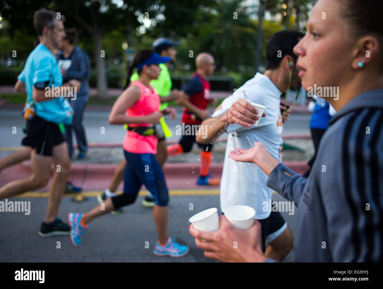 A volunteer offers cups of water to runners in the Miami Marathon in ...
