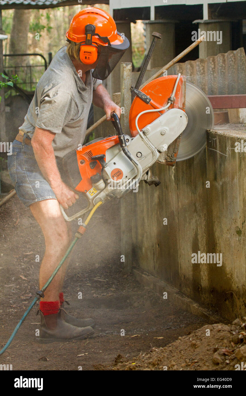 Man wearing ear & eye protection using brick / concrete saw to cut ...