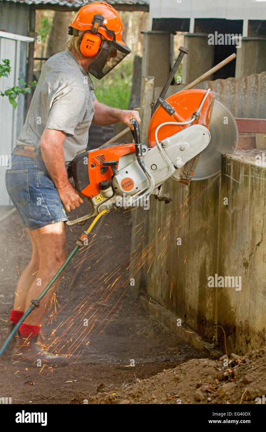 Man wearing ear & eye protection using brick / concrete saw to cut ...