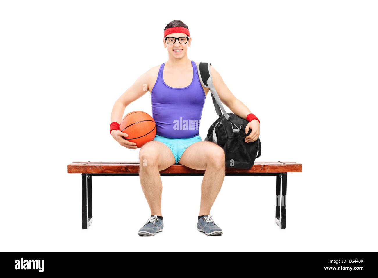 Nerdy athlete holding a basketball seated on a bench isolated on white ...
