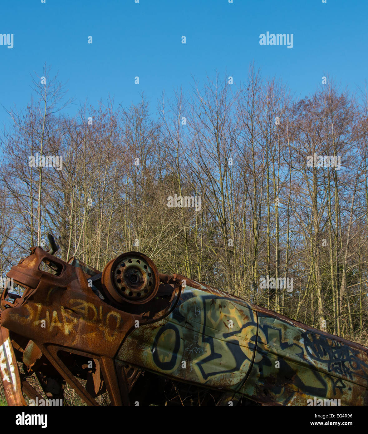 Wrecked rusty and graffiti covered car upturned in a field in front of ...